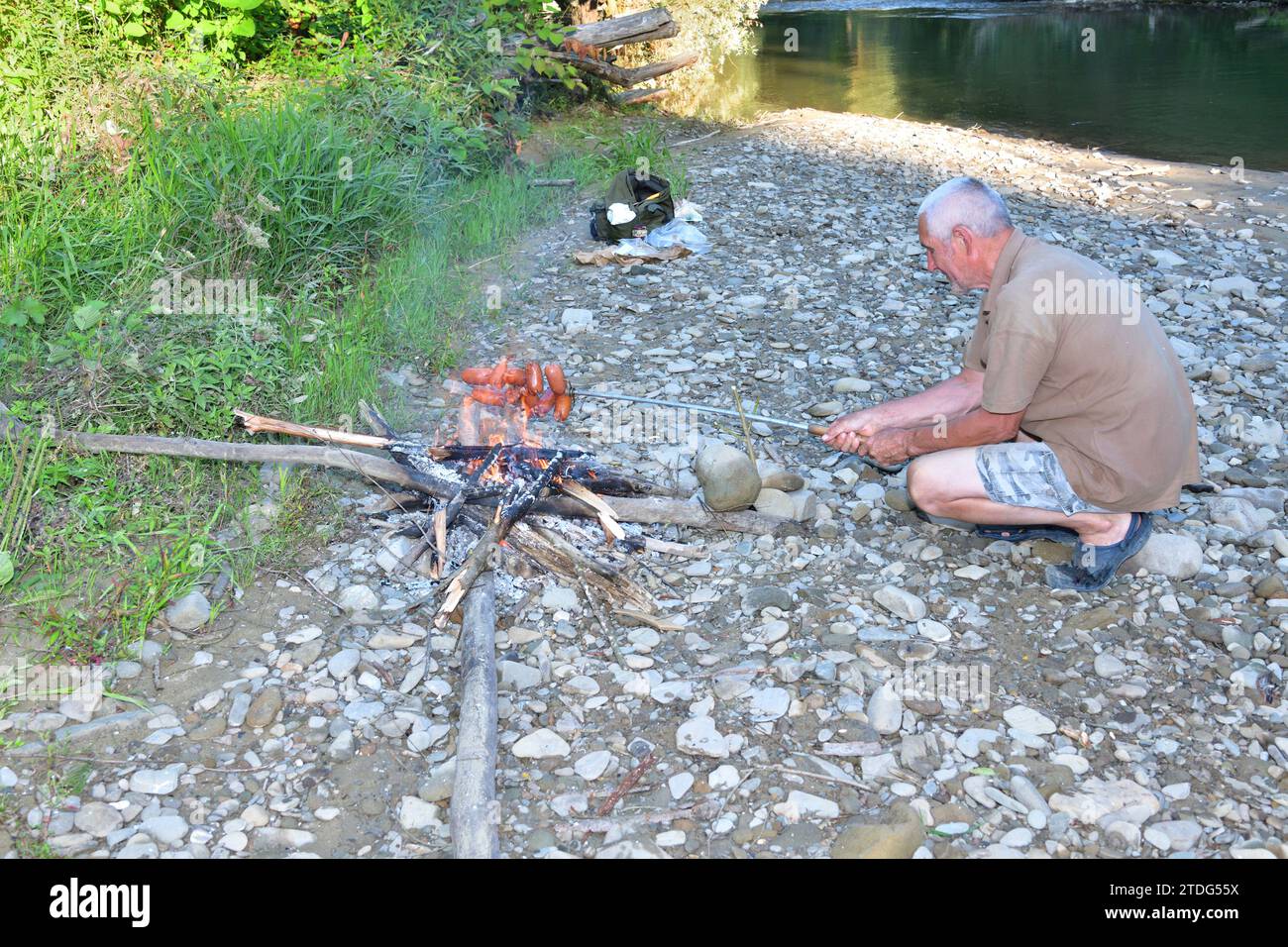 A man roasts a pile of sausages on a stick over a natural fire Stock ...