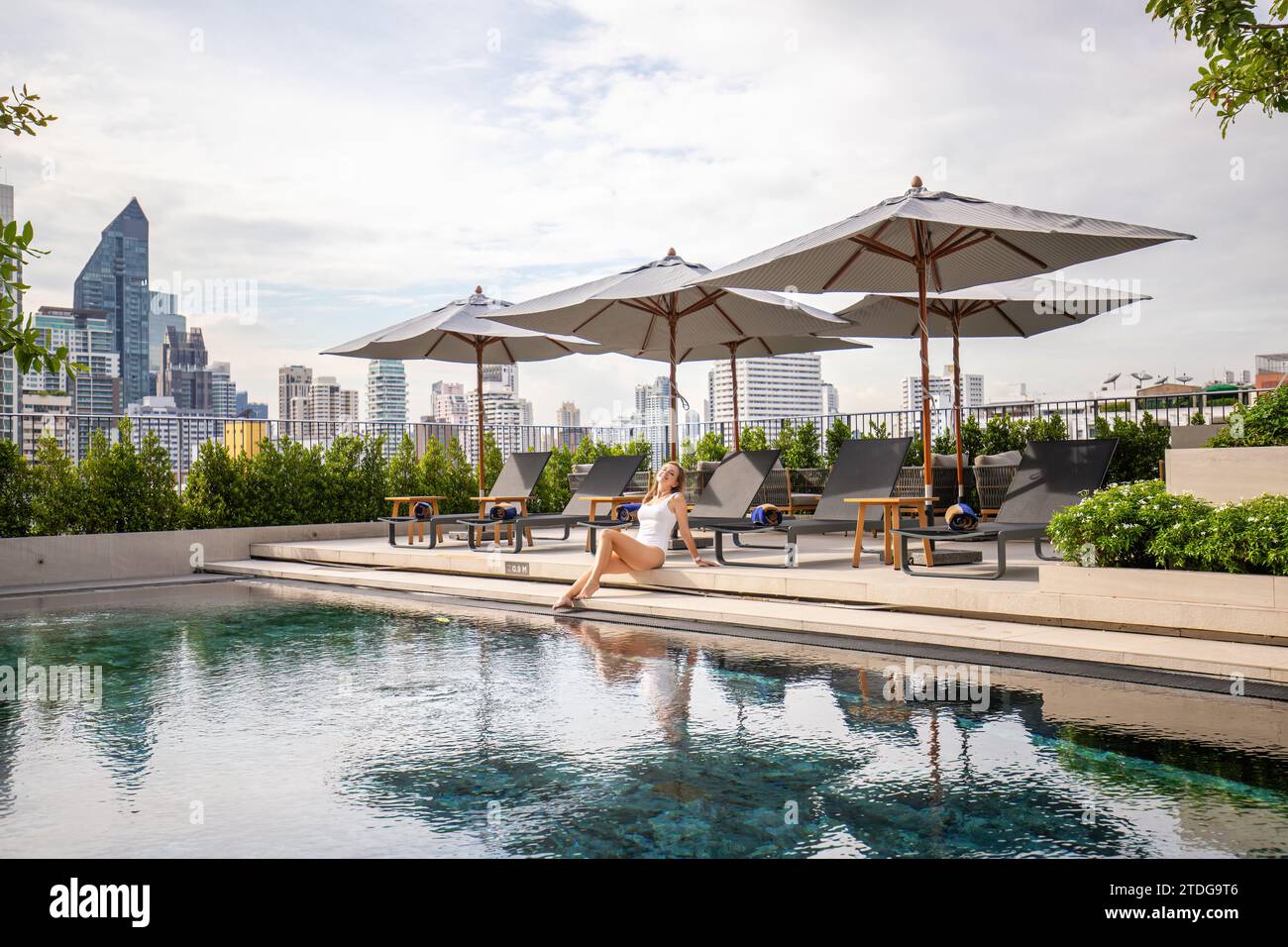 Woman relaxing at luxury rooftop pool with city skyline. Urban leisure ...