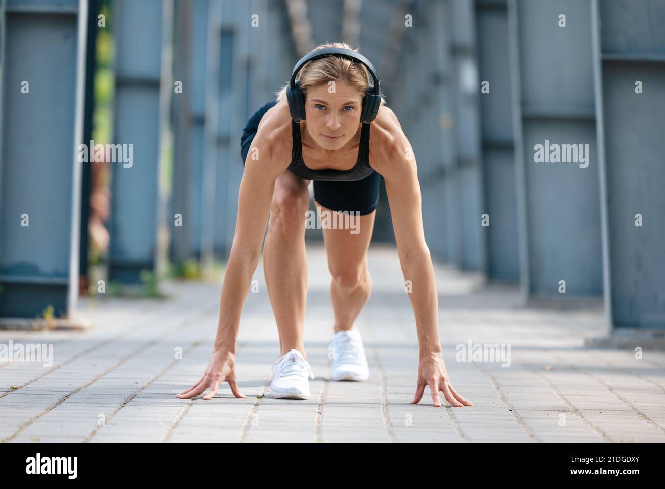 Woman ready for running standing in starting line pose wears wireless ...