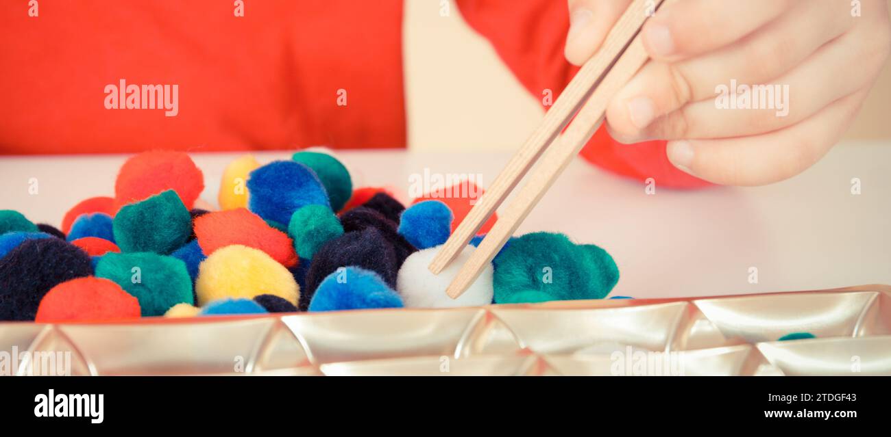 Preschooler playing with small colorful pompoms and wooden tongs ...
