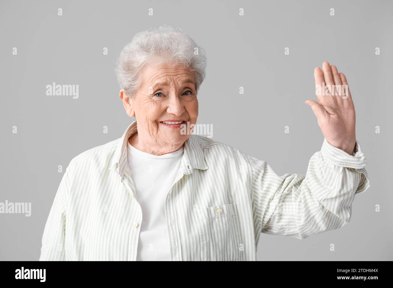 Senior woman waving hand on grey background Stock Photo - Alamy