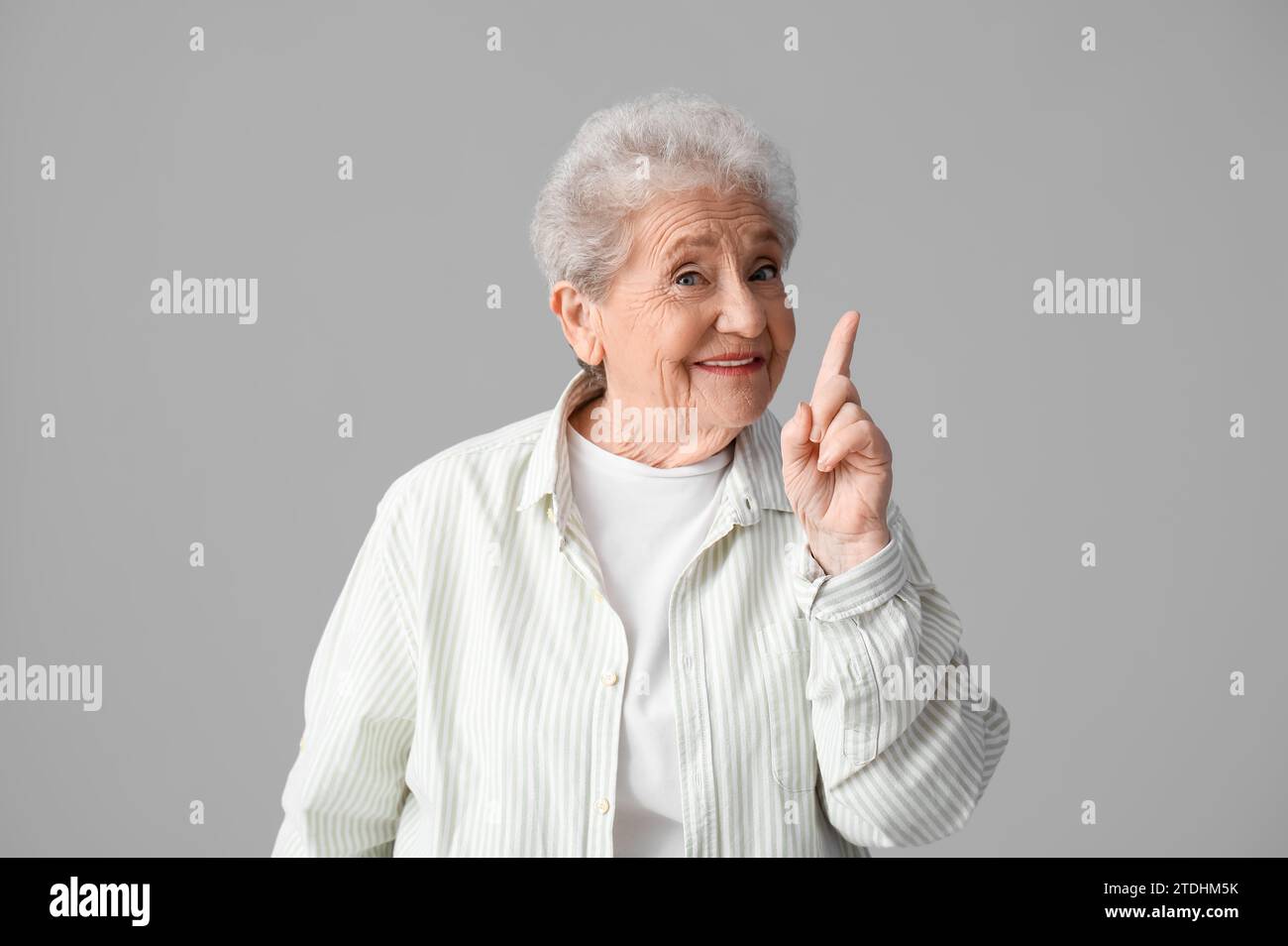 Senior woman pointing at something on grey background Stock Photo - Alamy