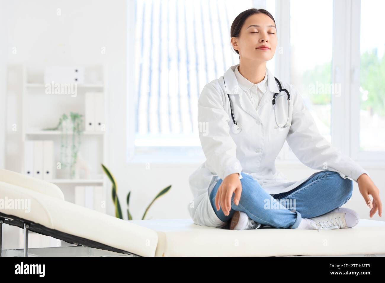 Female Asian doctor meditating on couch in clinic Stock Photo - Alamy