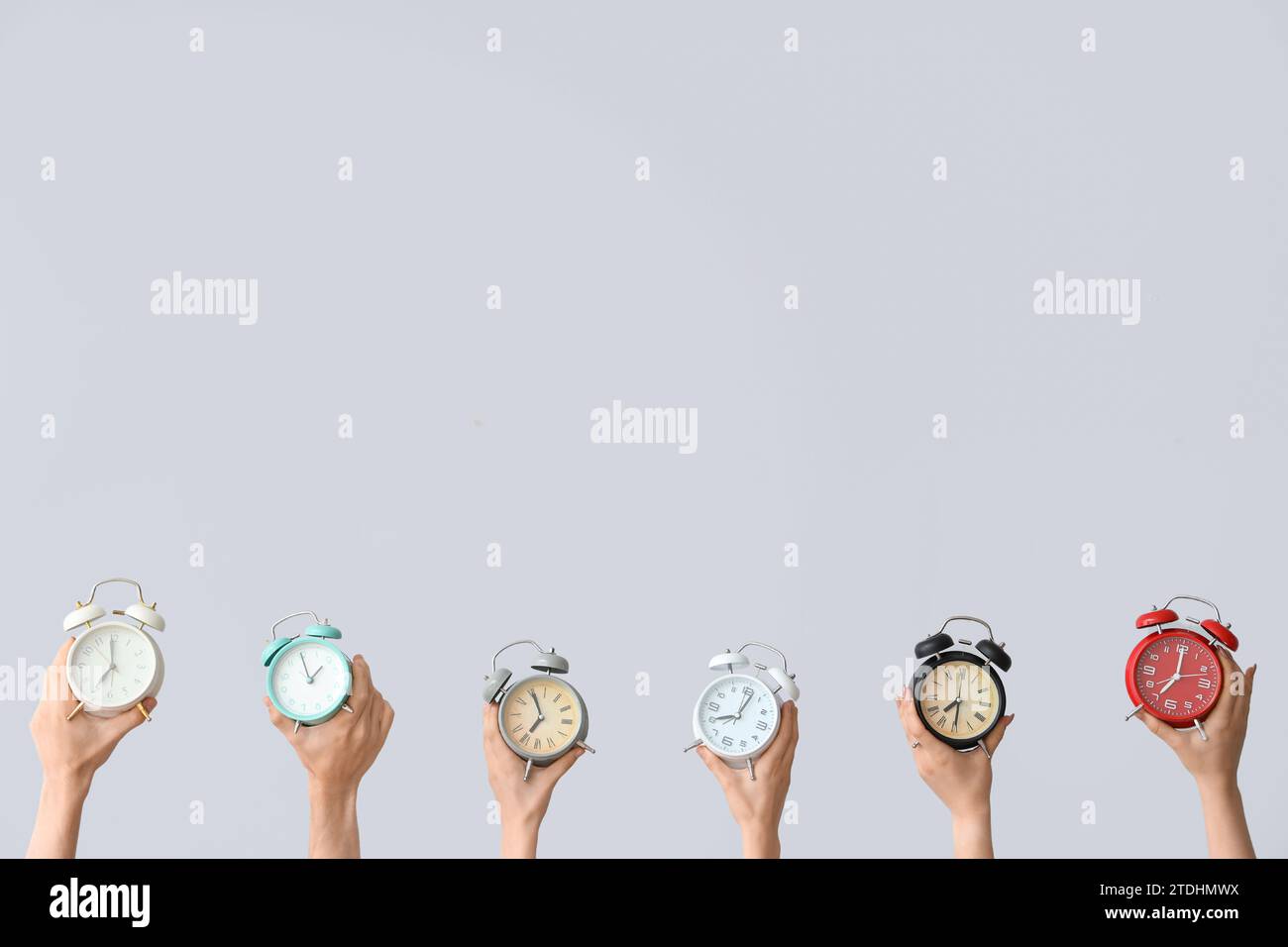 Hands holding different alarm clocks on grey background Stock Photo - Alamy