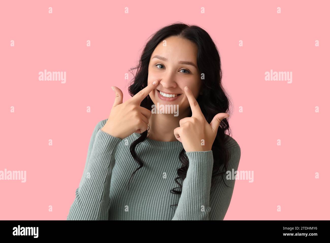 Portrait of pretty young woman pointing at her nose on pink background ...