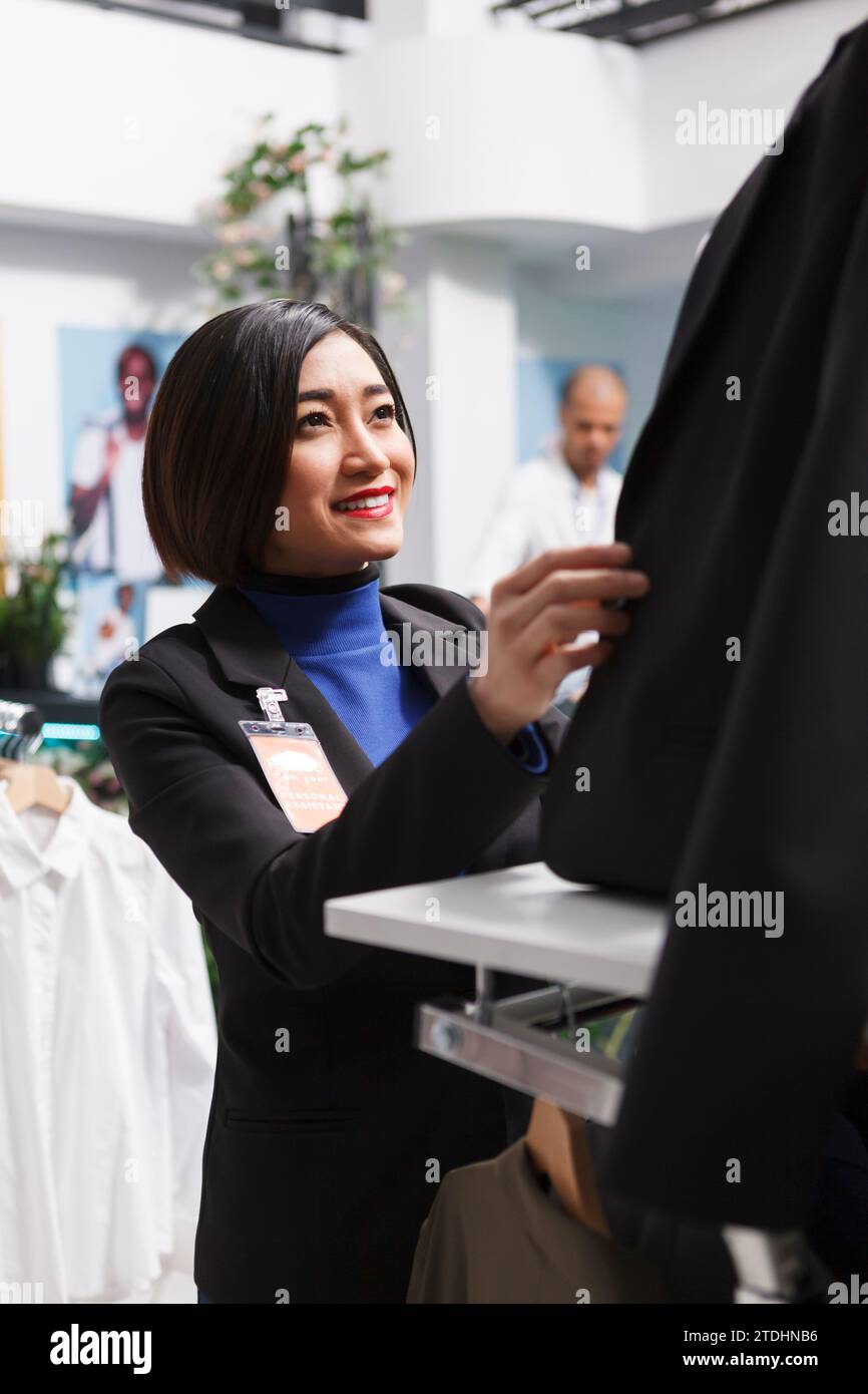 Clothing store smiling asian employee fastening jacket buttons while ...