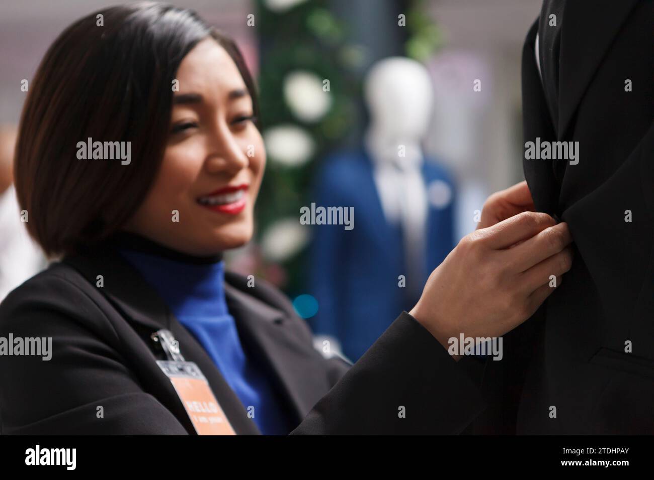 Clothing store smiling asian woman worker putting formal jacket on ...