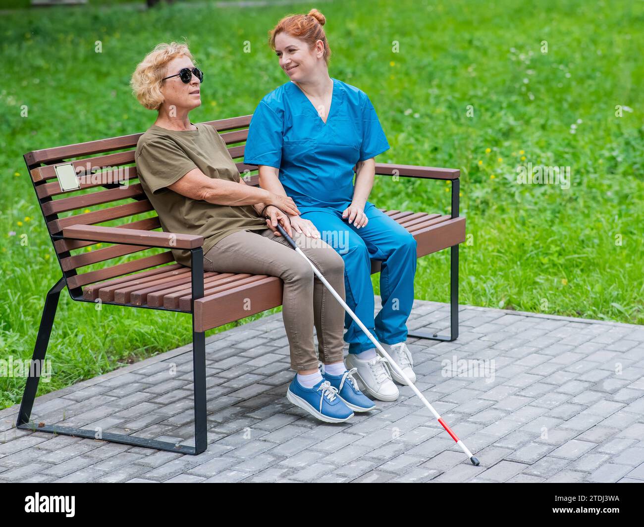 A nurse and an elderly blind woman are sitting on a bench in the park ...