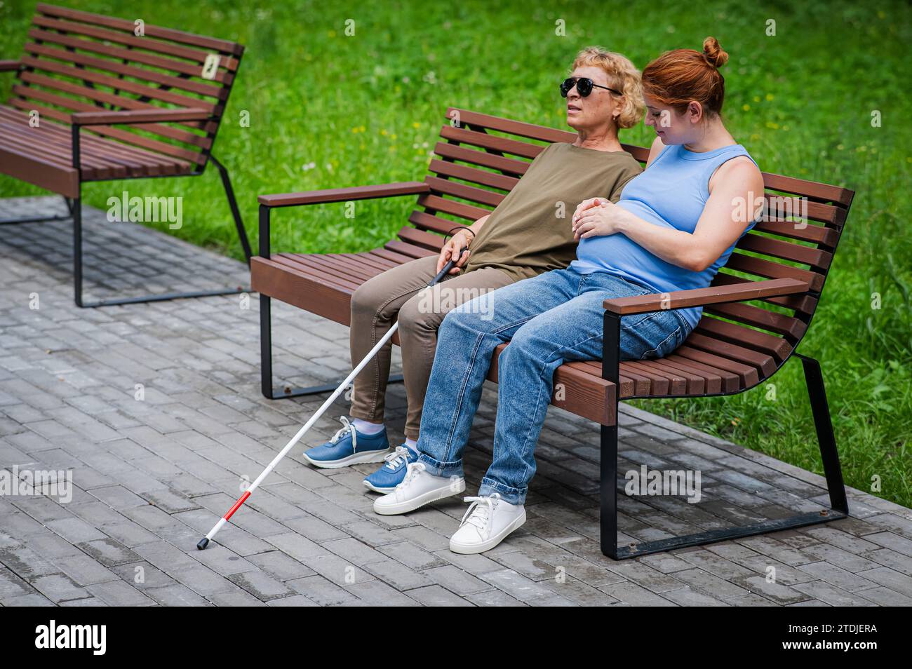 An elderly blind woman and her pregnant daughter are sitting on a bench ...