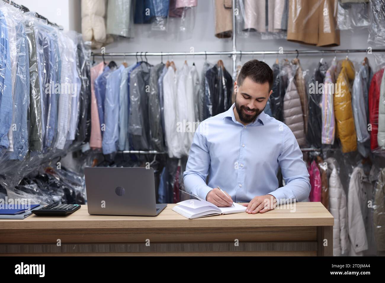 Dry-cleaning service. Happy worker taking notes at counter indoors ...