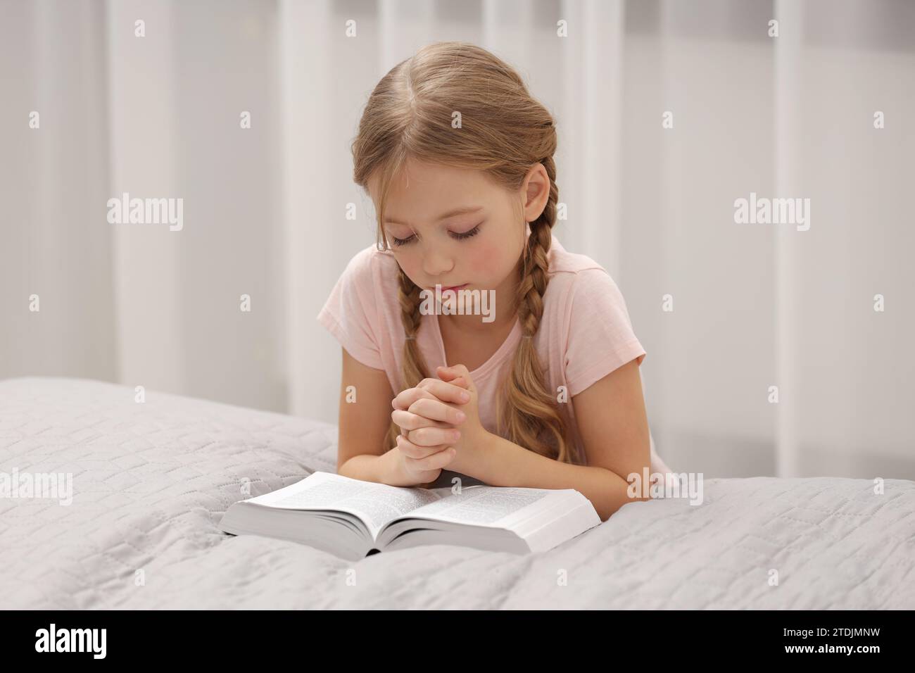 Girl holding hands clasped while praying over Bible in room Stock Photo ...