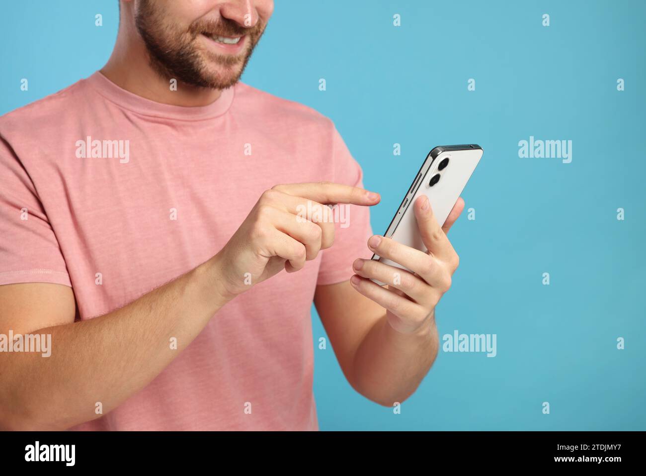 Man sending message via smartphone on light blue background, closeup ...