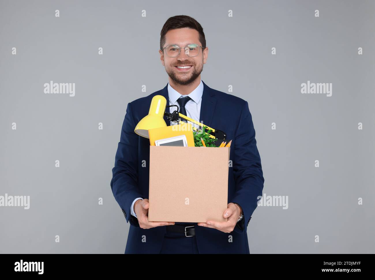 Happy unemployed man with box of personal office belongings on grey ...