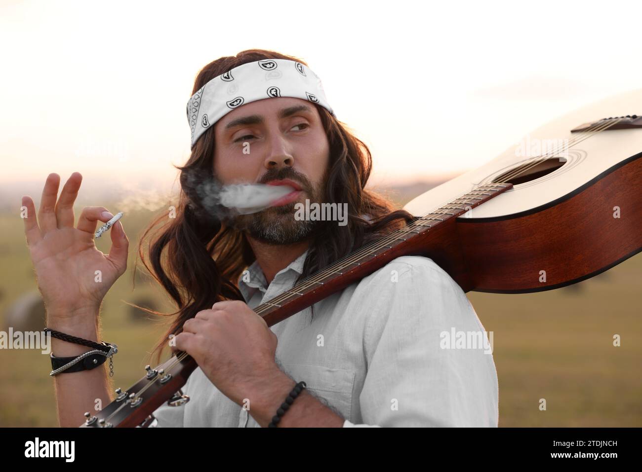 Stylish hippie man with guitar smoking joint in field Stock Photo - Alamy