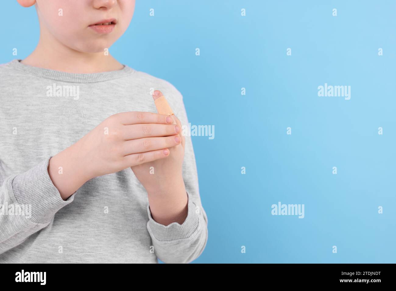 Little boy putting sticking plaster onto finger against light blue ...