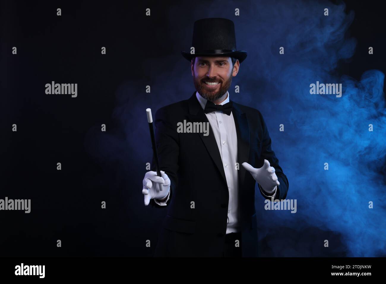 Happy magician holding wand in smoke on dark background Stock Photo - Alamy