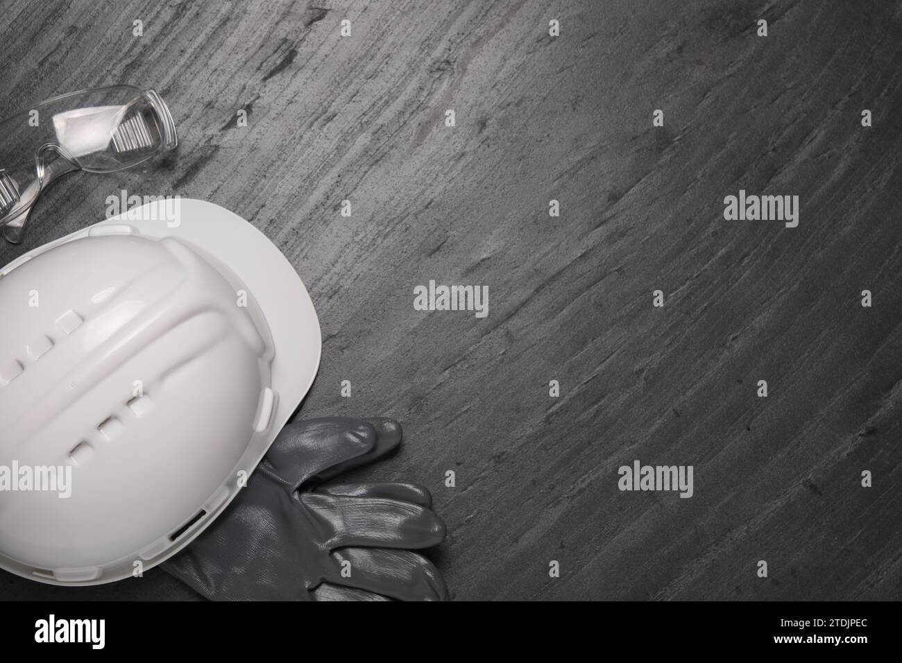 Hard hat, gloves and goggles on black table, flat lay with space for ...