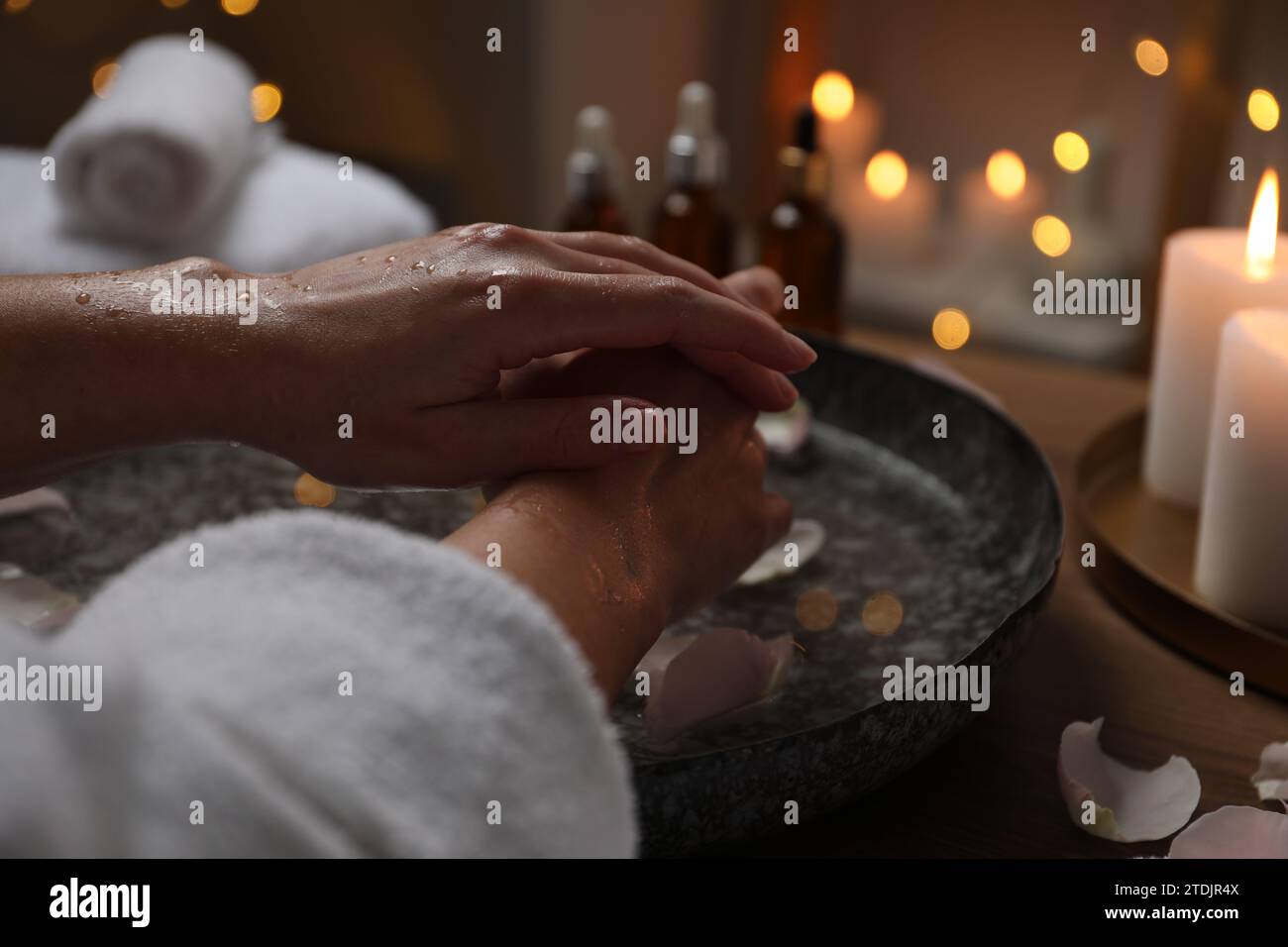 Woman soaking her hands in bowl of water and flower petals at table ...