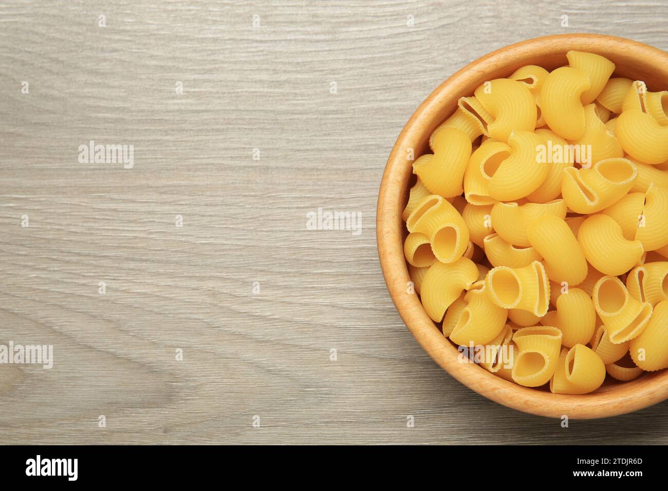 Raw macaroni pasta in bowl on light grey wooden table, top view. Space ...