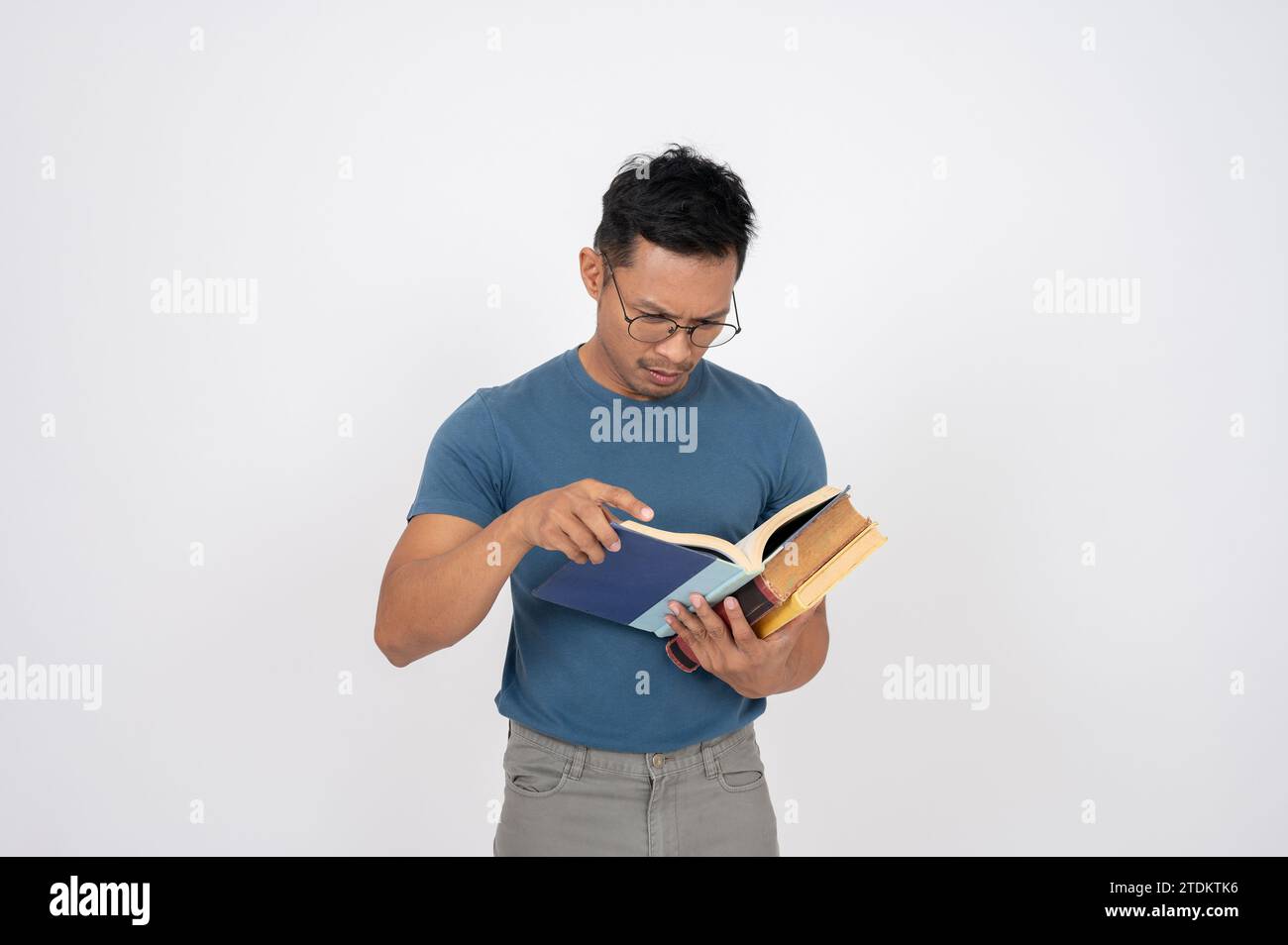 A stressed, serious Asian man is focusing on reading a book while ...