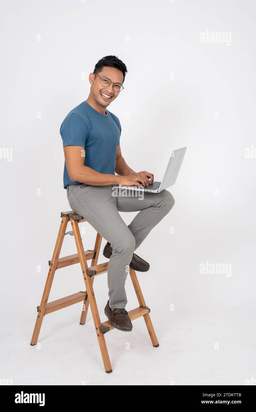 A smart and positive Asian man in casual clothes is using his laptop ...