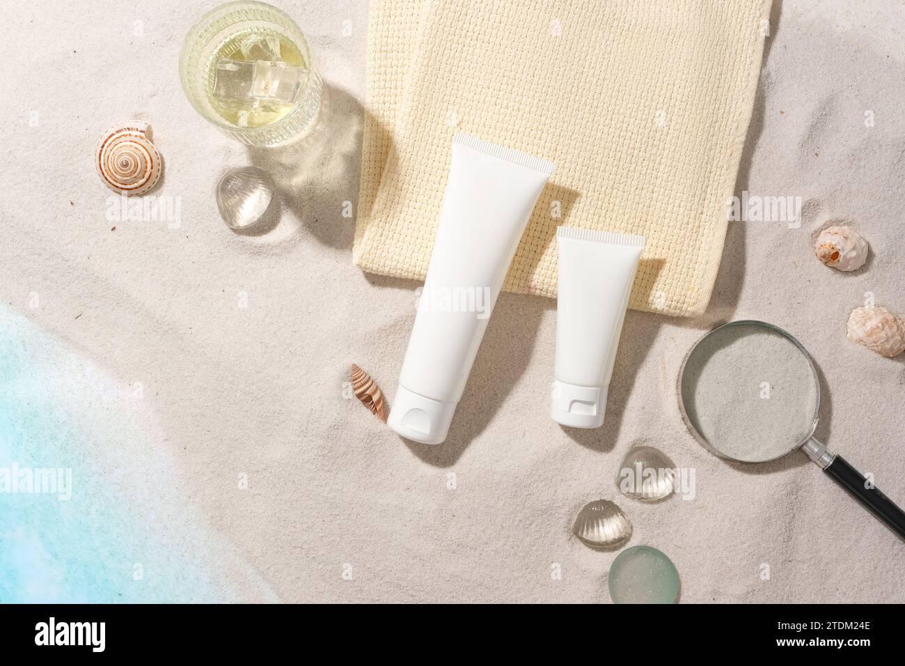 Top view of two white cosmetic tubes, seashells, a magnifying glass, a towel and glass balls ...