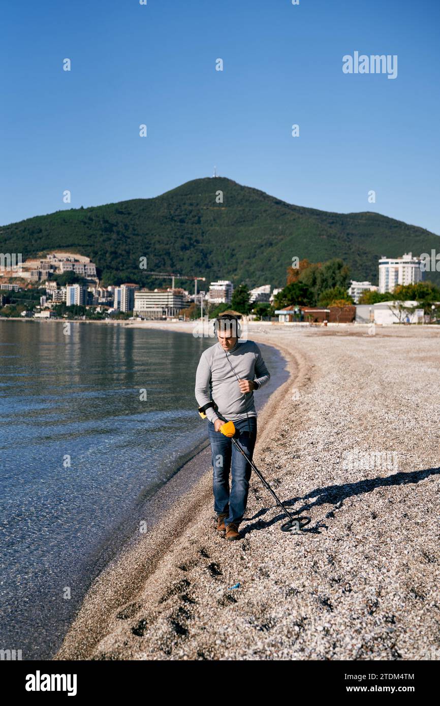 Beach cop in headphones walks with a metal detector along the shore by ...