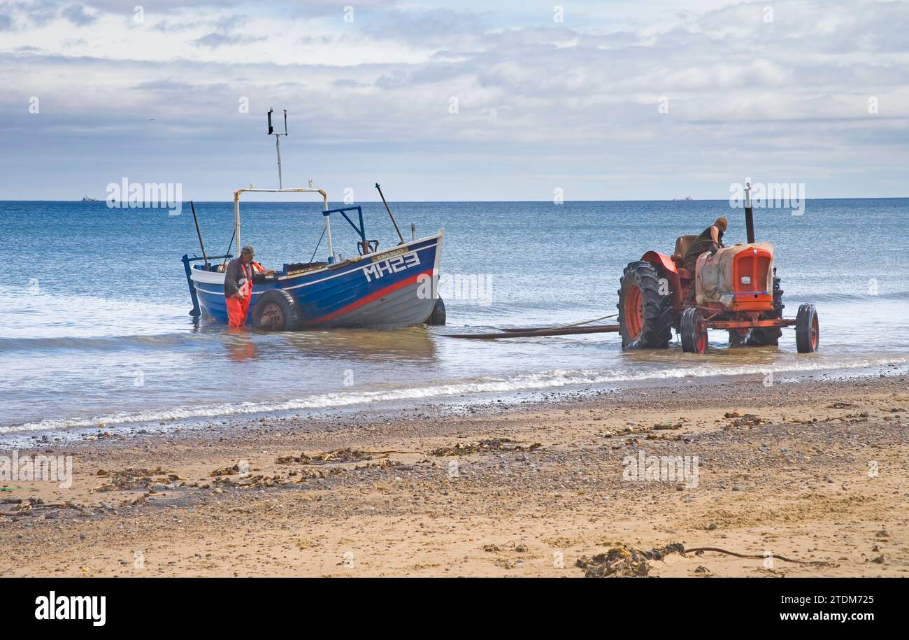 tractors pulling fishing boats from the sea on the beach at marske by ...