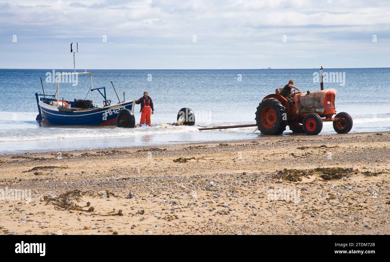 tractors pulling fishing boats from the sea on the beach at marske by ...