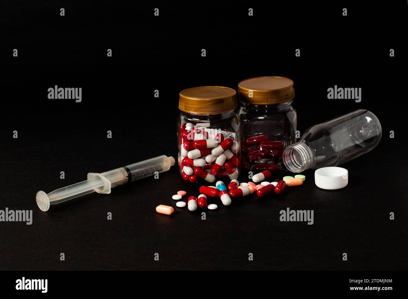 Medicine in a bottle, scattered outside the bottle and nearby a syringe ...