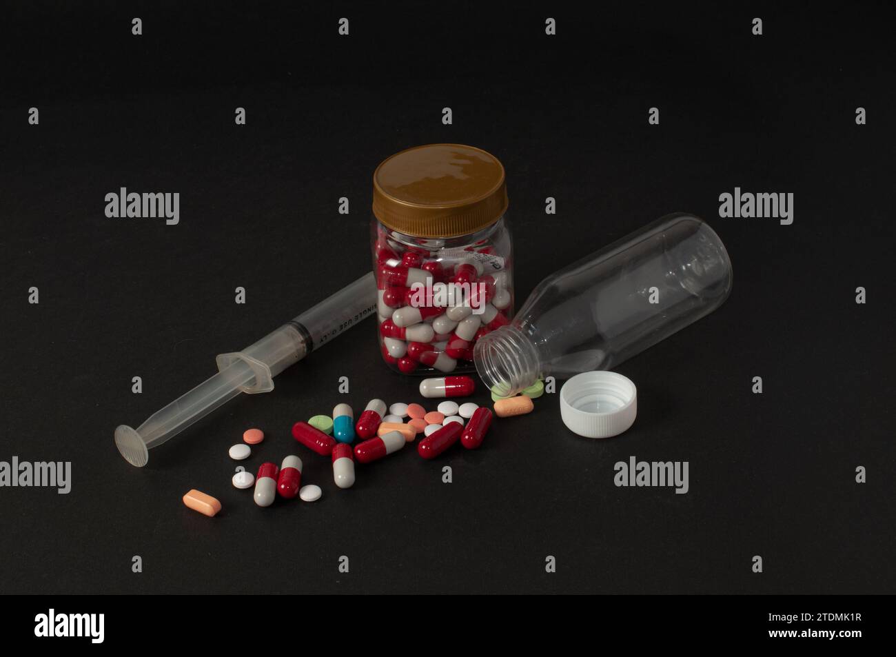 Medicine in a bottle, scattered outside the bottle and nearby a syringe ...