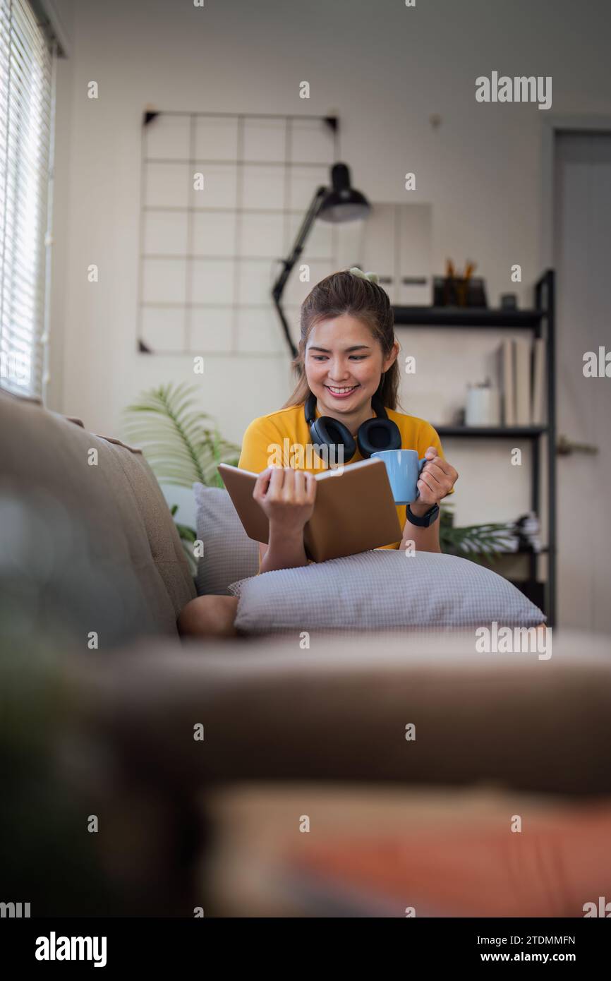 Happy young woman read book on sofa at home. Lifestyle freelance relax ...