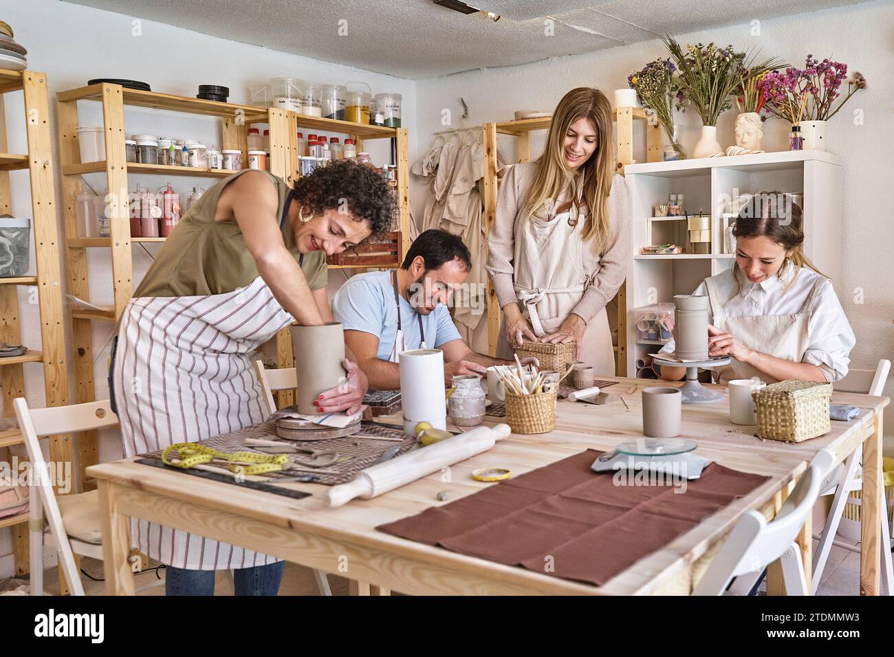 Enthusiastic group of four shaping clay in a well-lit pottery studio ...