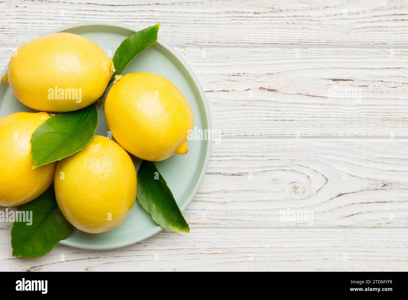 Fresh cutted lemon and whole lemons over round plate on colored ...