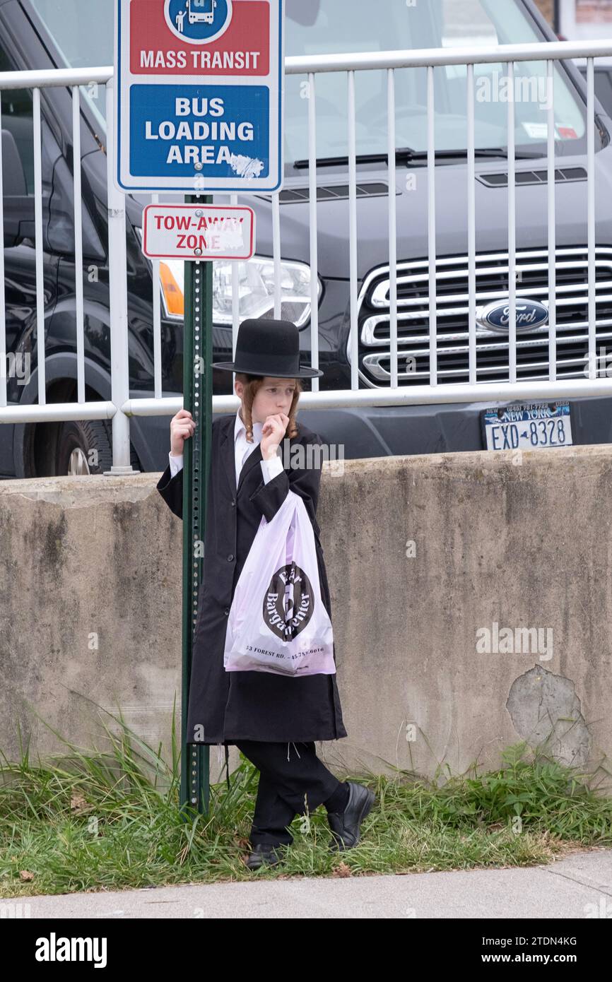An orthodox Jewish boy with long peyus waits for a bus on Forest Road ...