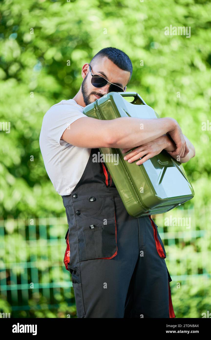 Handsome worker hugging tightly canister full of gasoline. Young gas ...