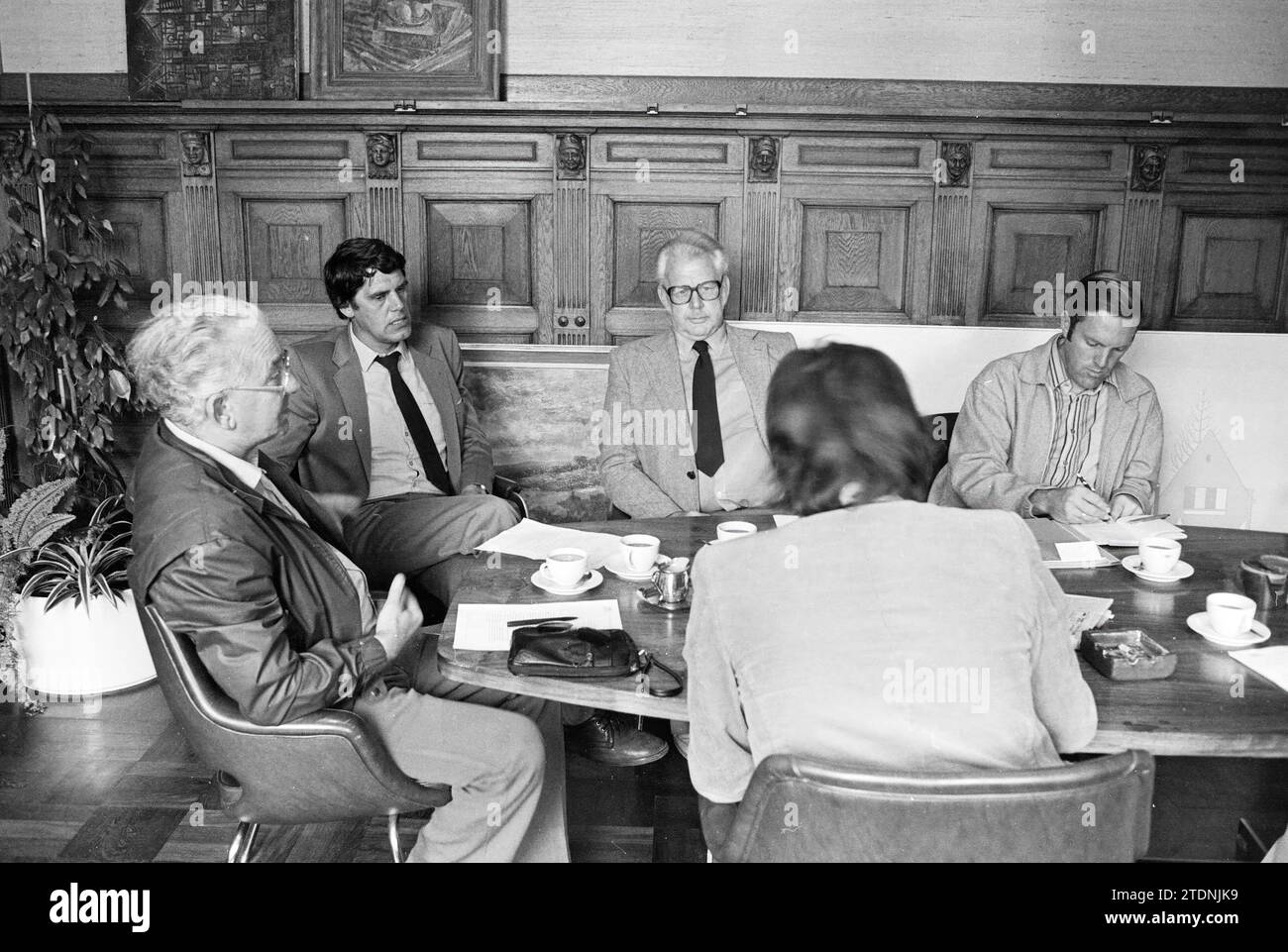 Five men around a conference table in a room with wood paneling ('press ...