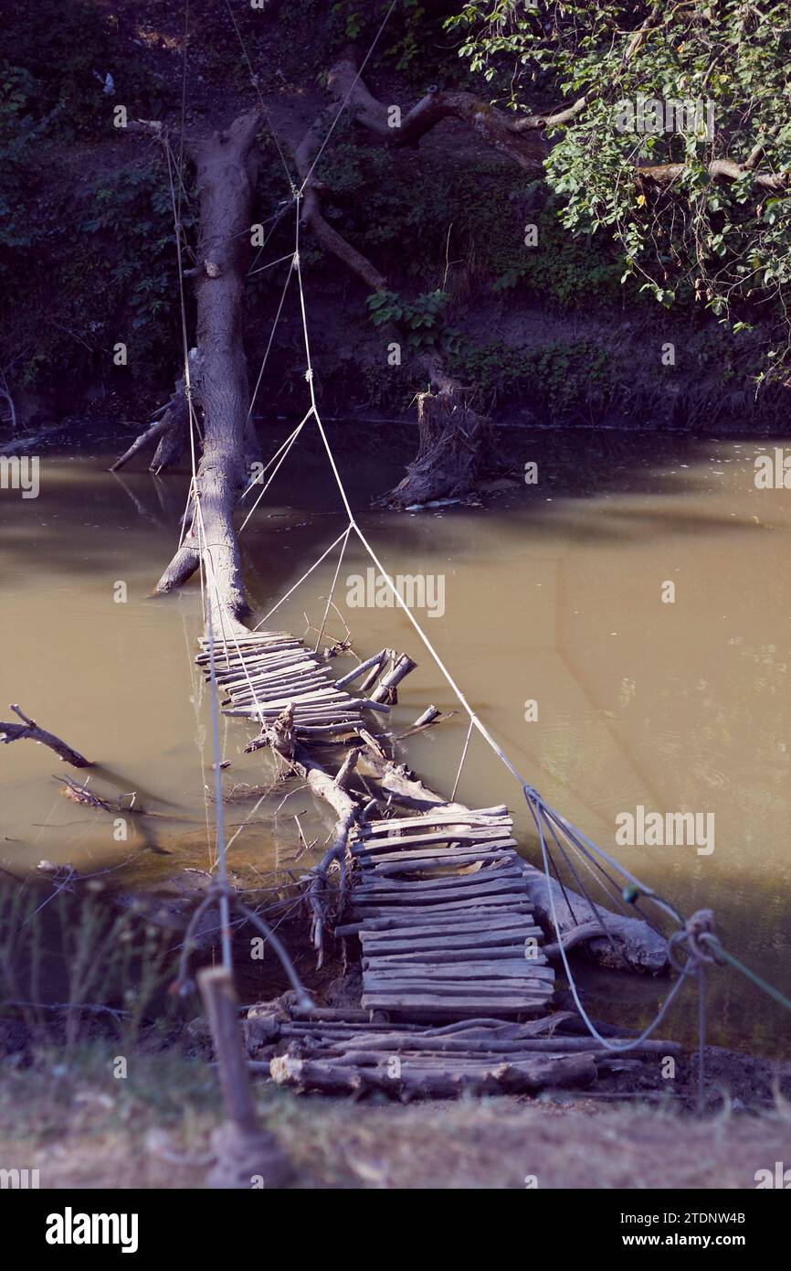 A homemade wooden bridge built over a river with railings made of ropes ...