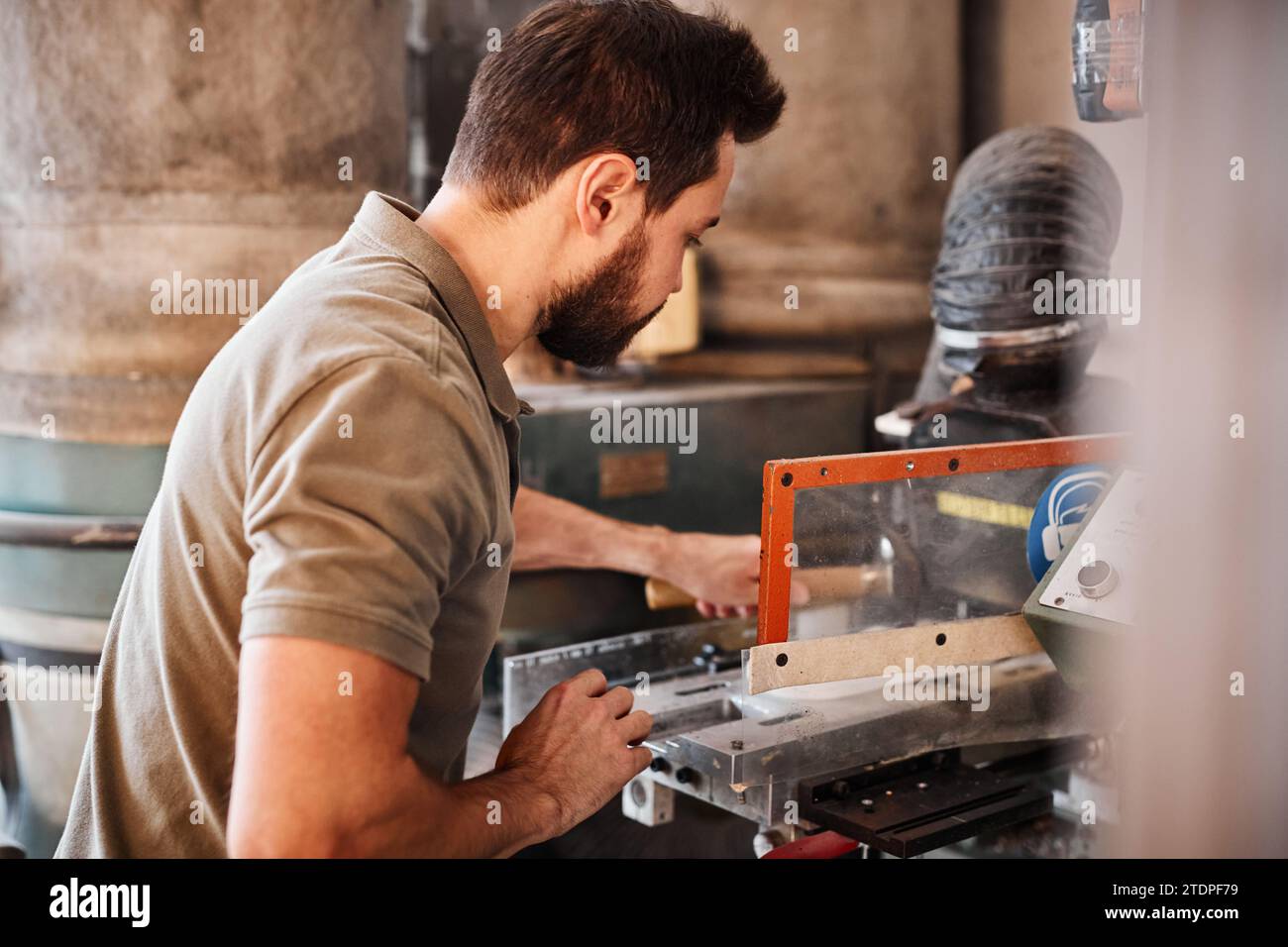 Side view of young male leatherworker with hammer standing by ...