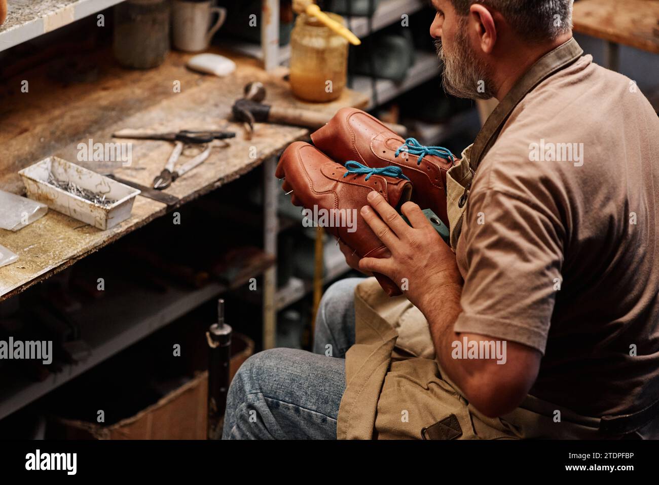 Side view of mature professional shoemaker holding brown leather ...