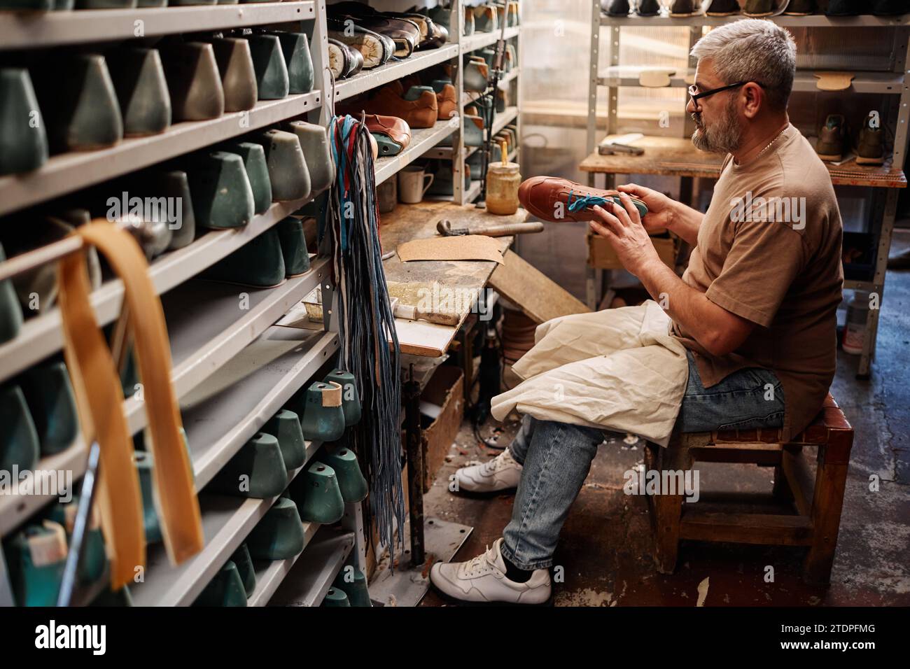 Side view of mature professional shoemaker holding brown boot workpiece ...