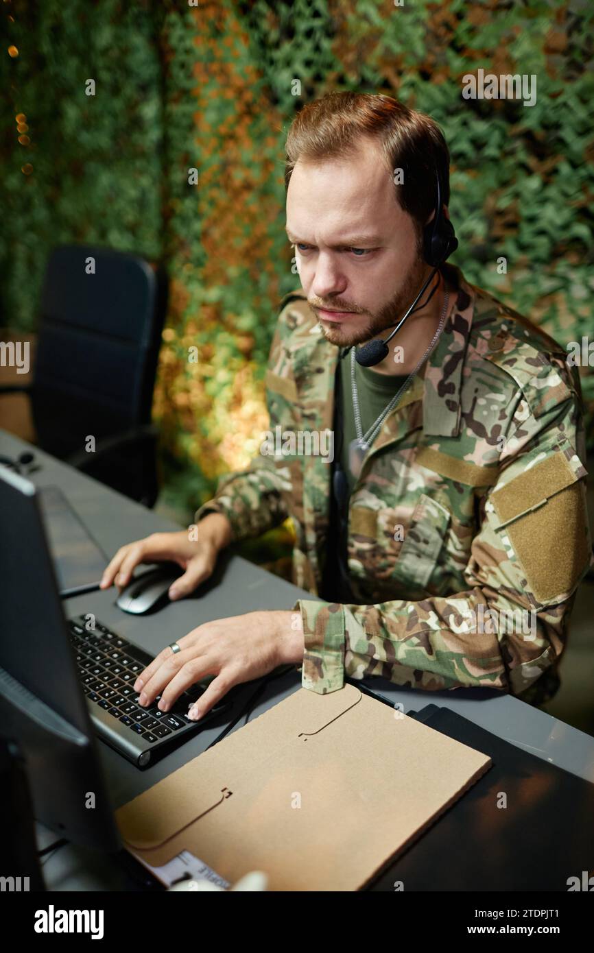Young serious male military officer in headset keeping hand on computer ...
