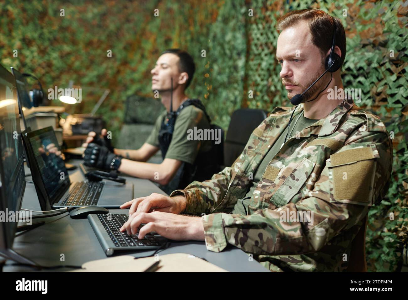 Serious young male operator in camouflage uniform typing on computer ...
