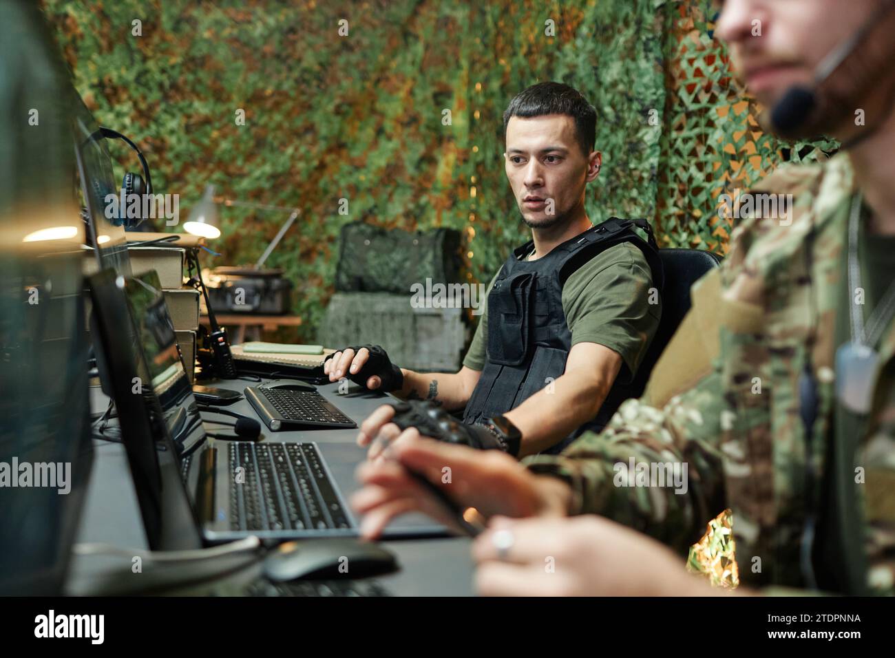 Young serious male military officer in protective body armor sitting by ...