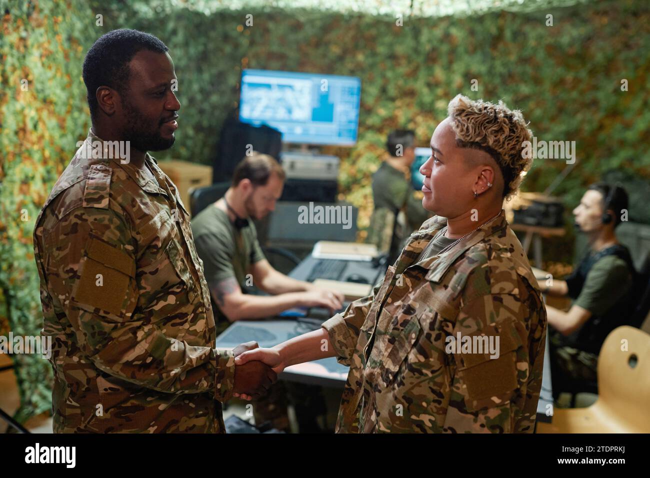 Two young intercultural officers in camouflage uniform shaking hands ...