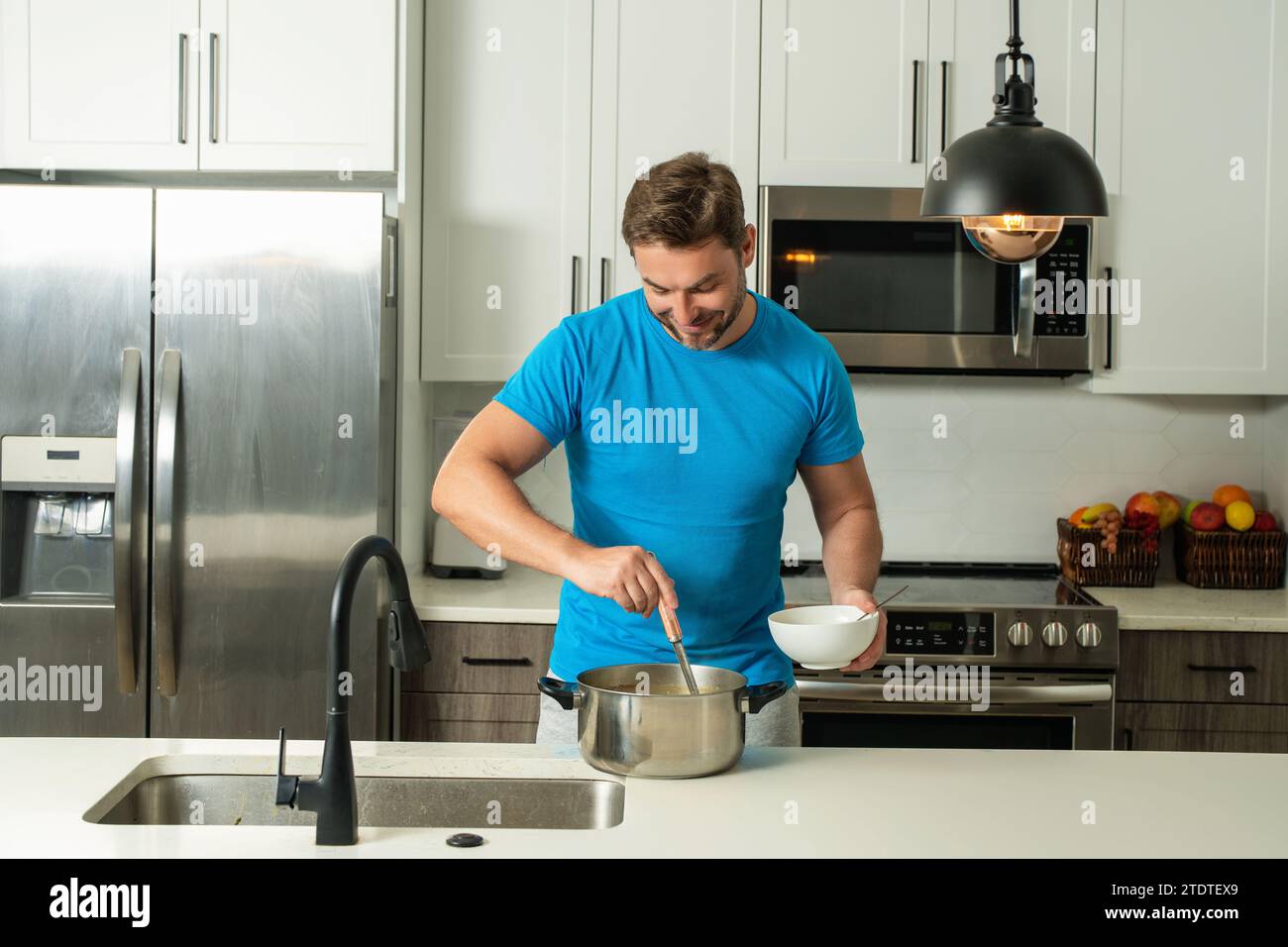 Man cooking at kitchen. Handsome man preparing delicious meal in modepn ...
