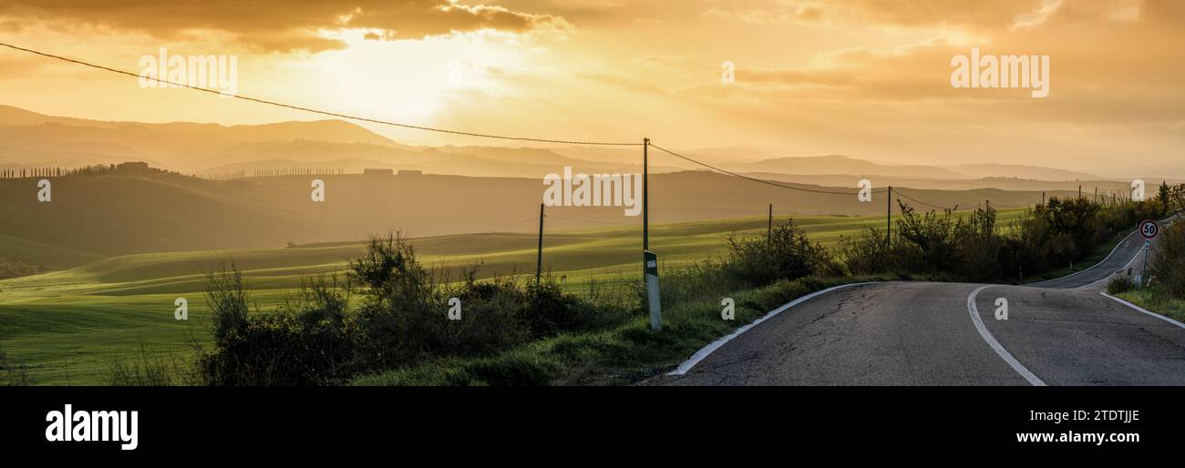 A panorama landscape with a curvy and hilly country road at sunrise in ...