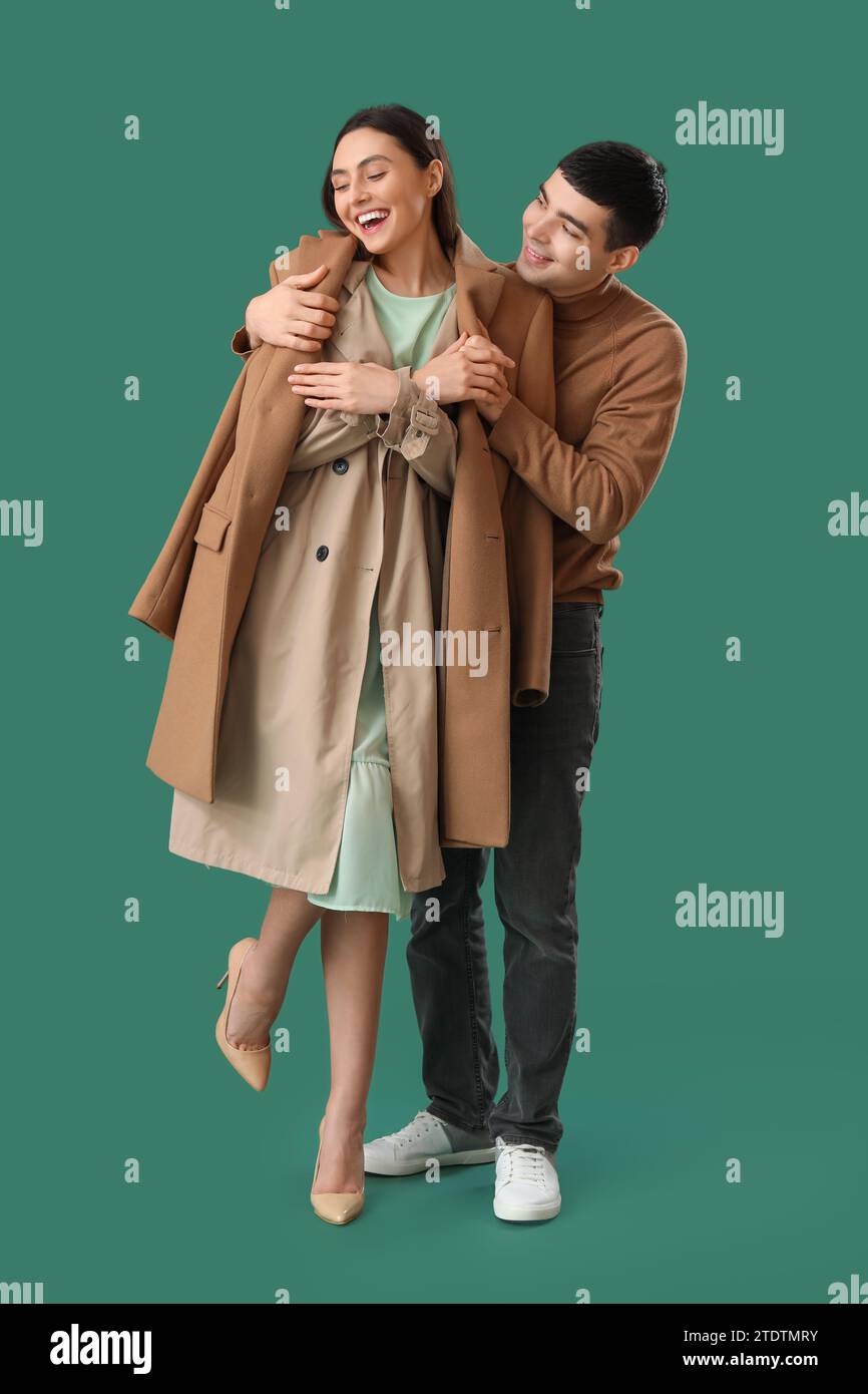 Young man putting coat onto his girlfriend on green background Stock ...