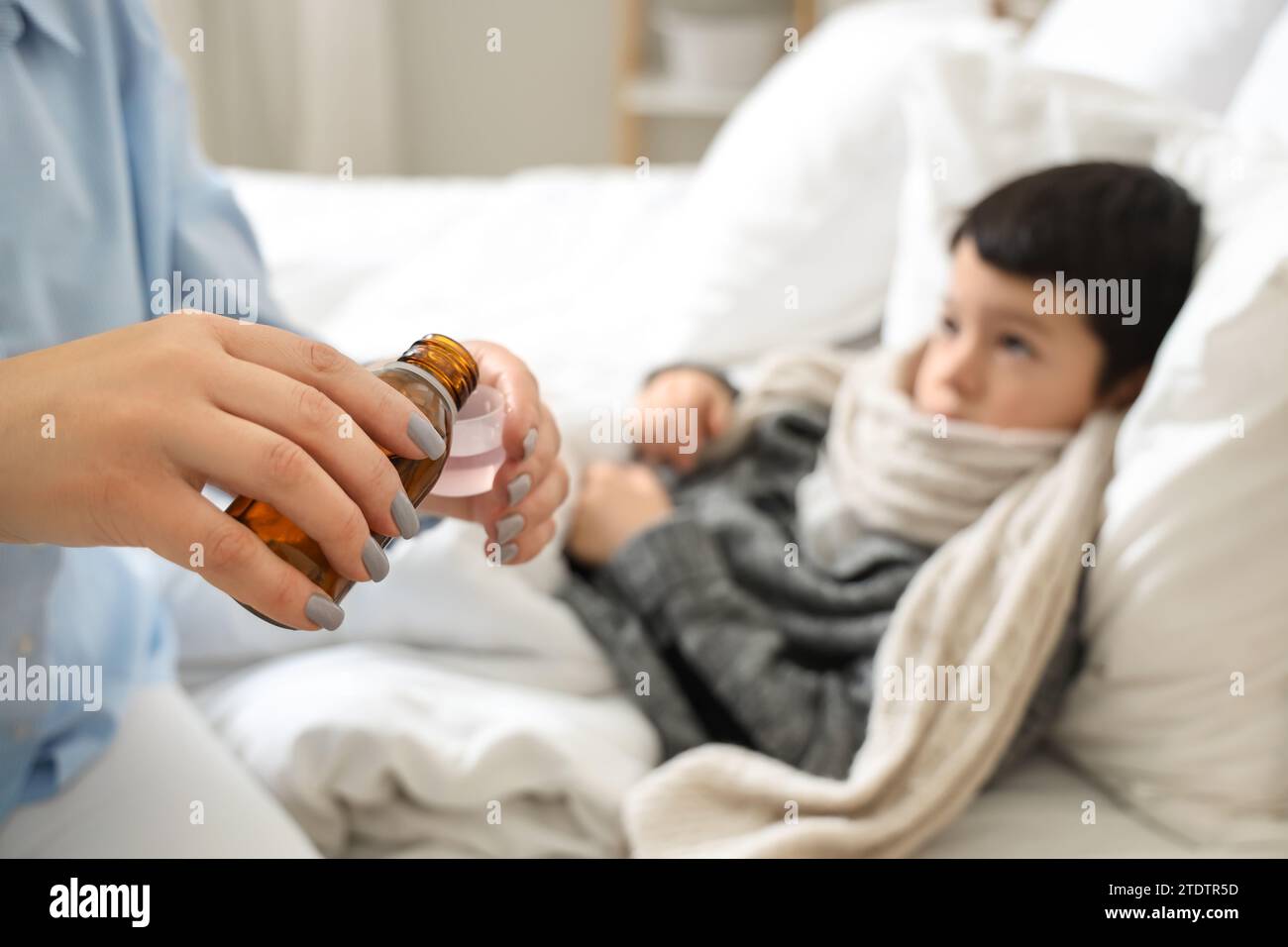 Mother pouring cough syrup for her ill little son in bedroom, closeup ...
