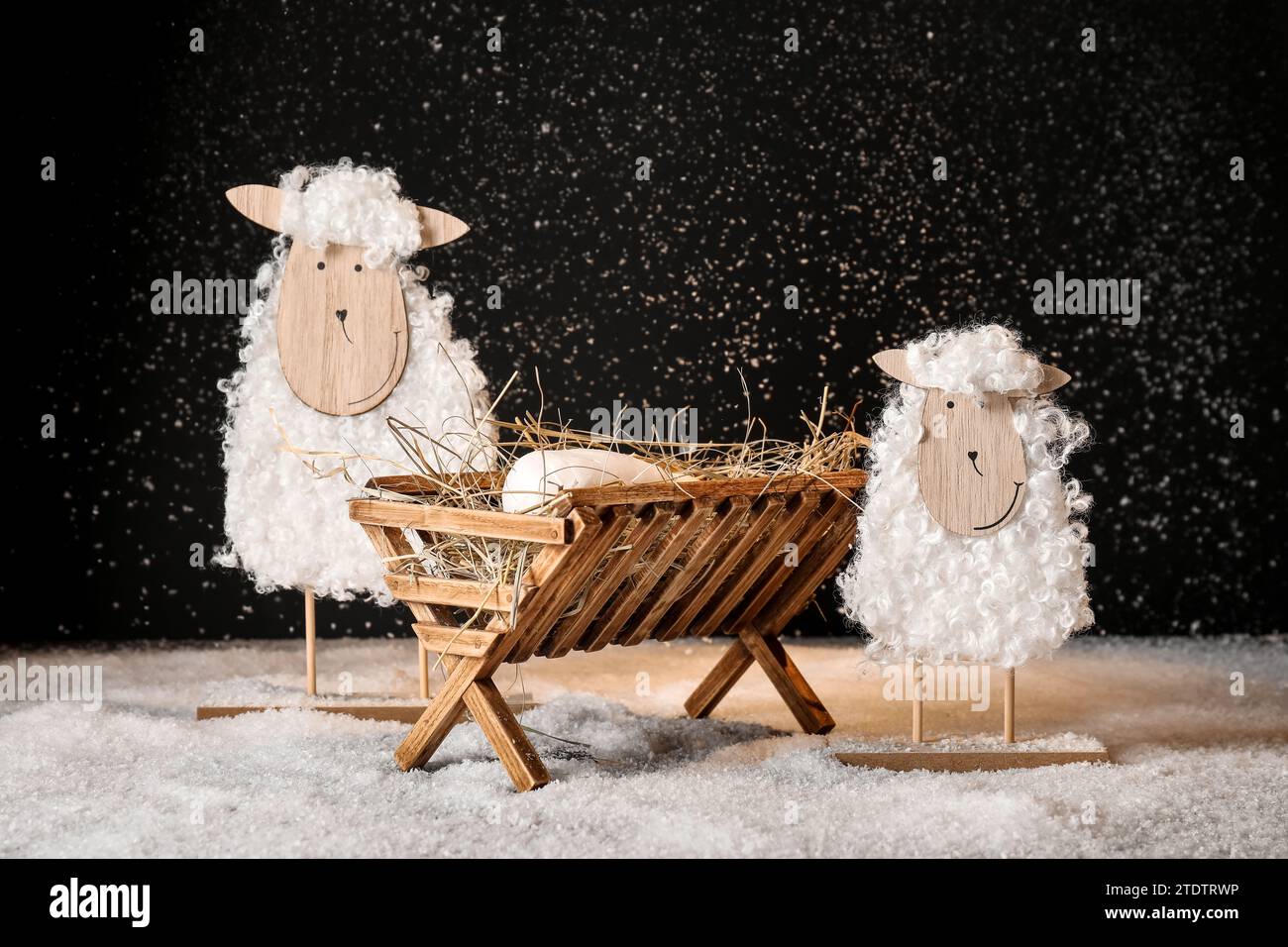 Toy sheep and wooden manger with dummy of baby on snow against black ...